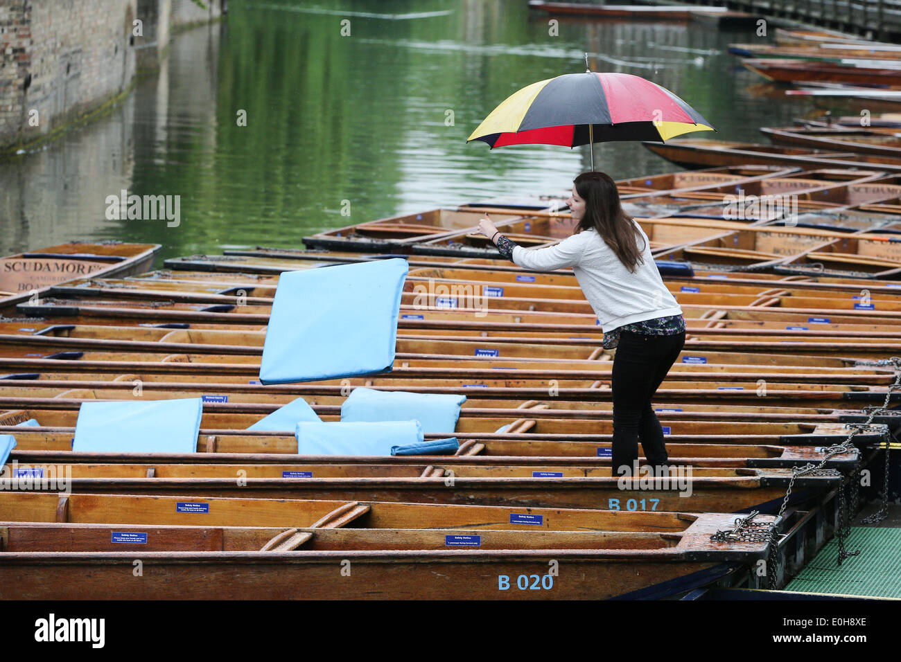 GIRL PUTTING OUT CUSHIONS ON A PUNT IN CAMBRIDGE HOLDING AN UMBRELLA IN ...