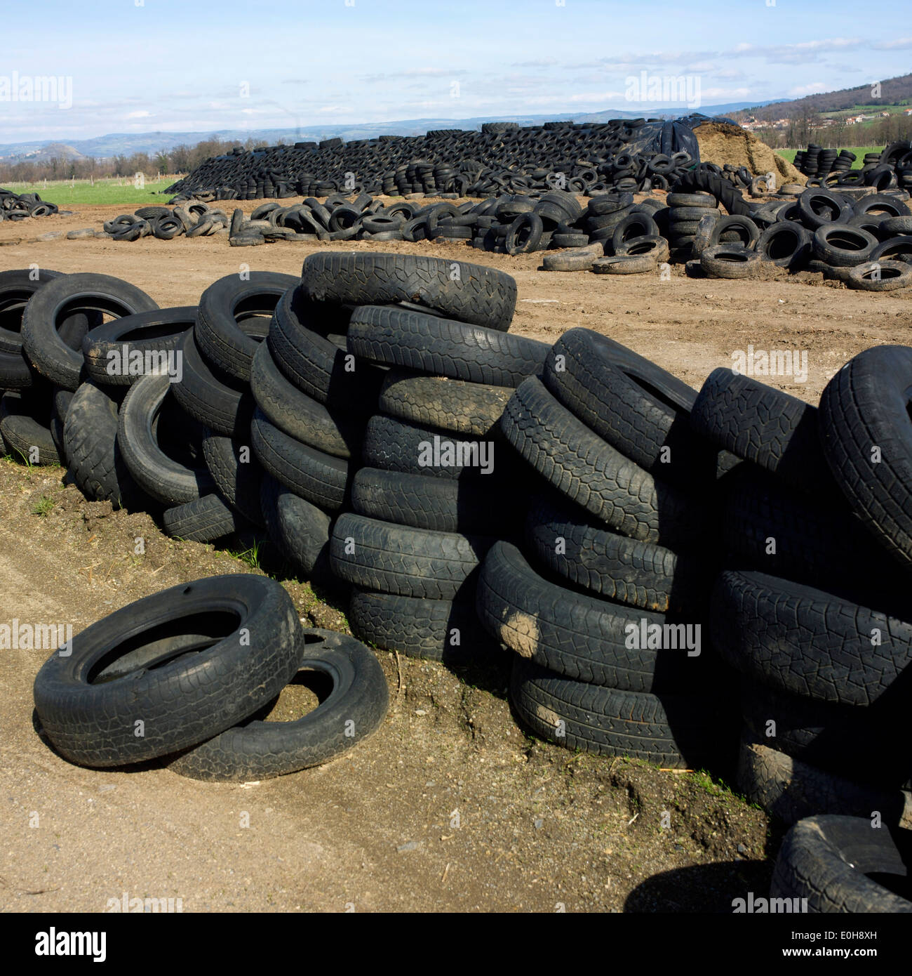 Discarded tires stacked in a recycling facility under clear blue sky ...