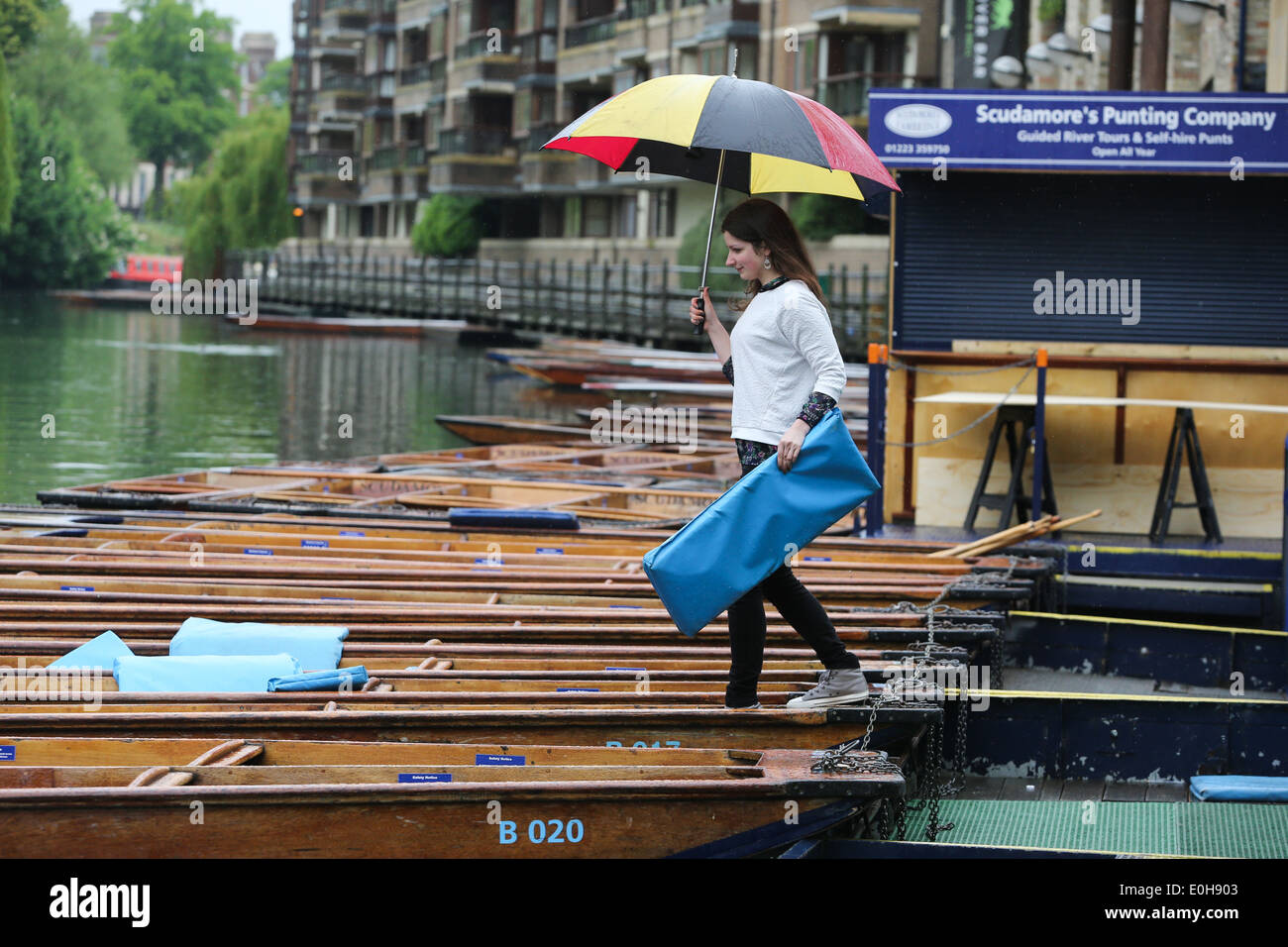 GIRL PUTTING OUT CUSHIONS ON A PUNT IN CAMBRIDGE HOLDING AN UMBRELLA IN ...