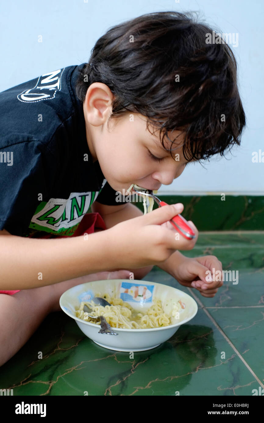 little boy enjoying a bowl of instant noodles outside of his home in ...