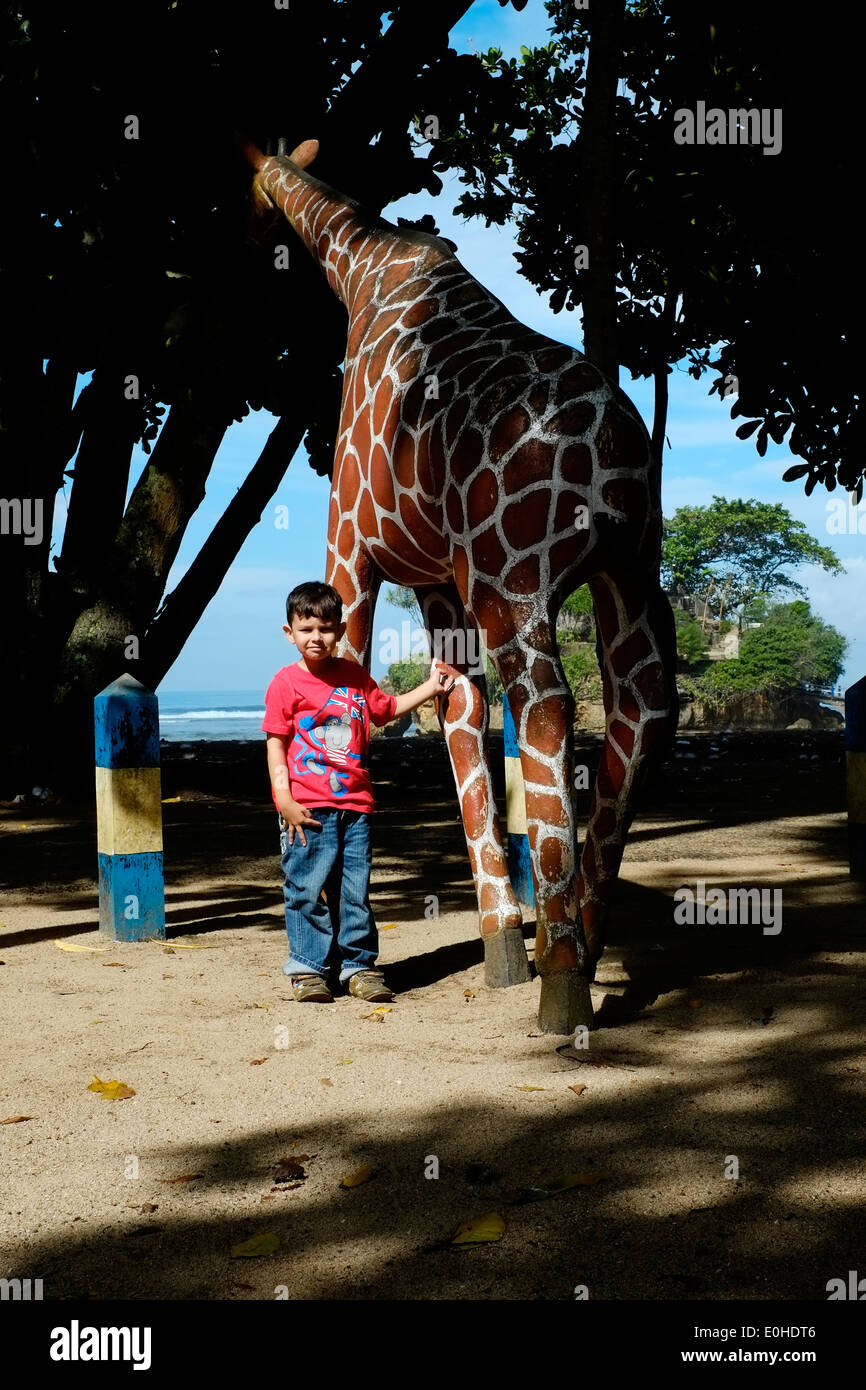 young local boy playing by giraffe statue by the beach and sea at ...