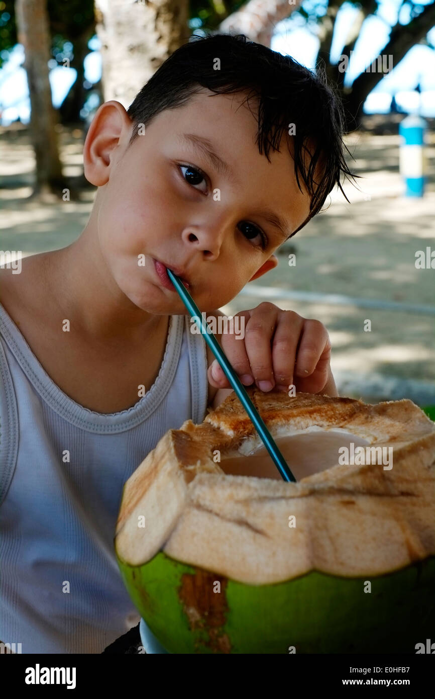 young boy drinking from fresh coconut by the beach and sea at ...