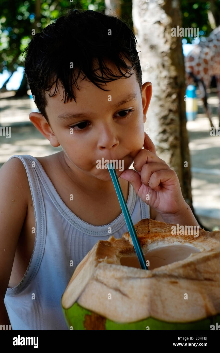 young boy drinking from fresh coconut by the beach and sea at balekambang east java indonesia ...