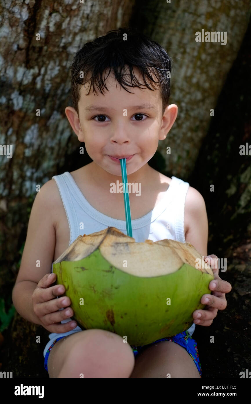 young boy drinking from fresh coconut by the the beach and sea at ...