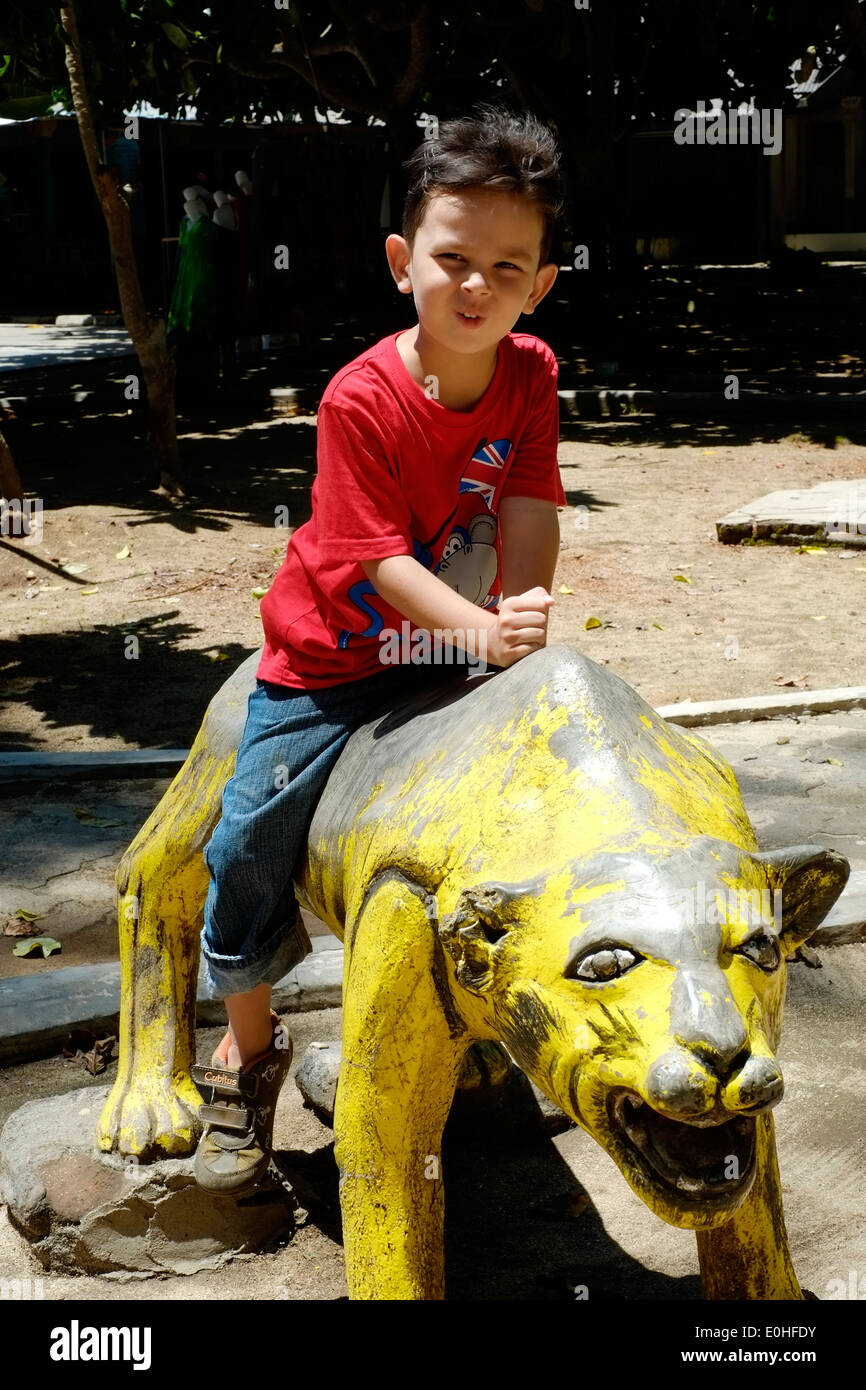 young boy riding on sculpture by the the beach and sea at balekambang ...