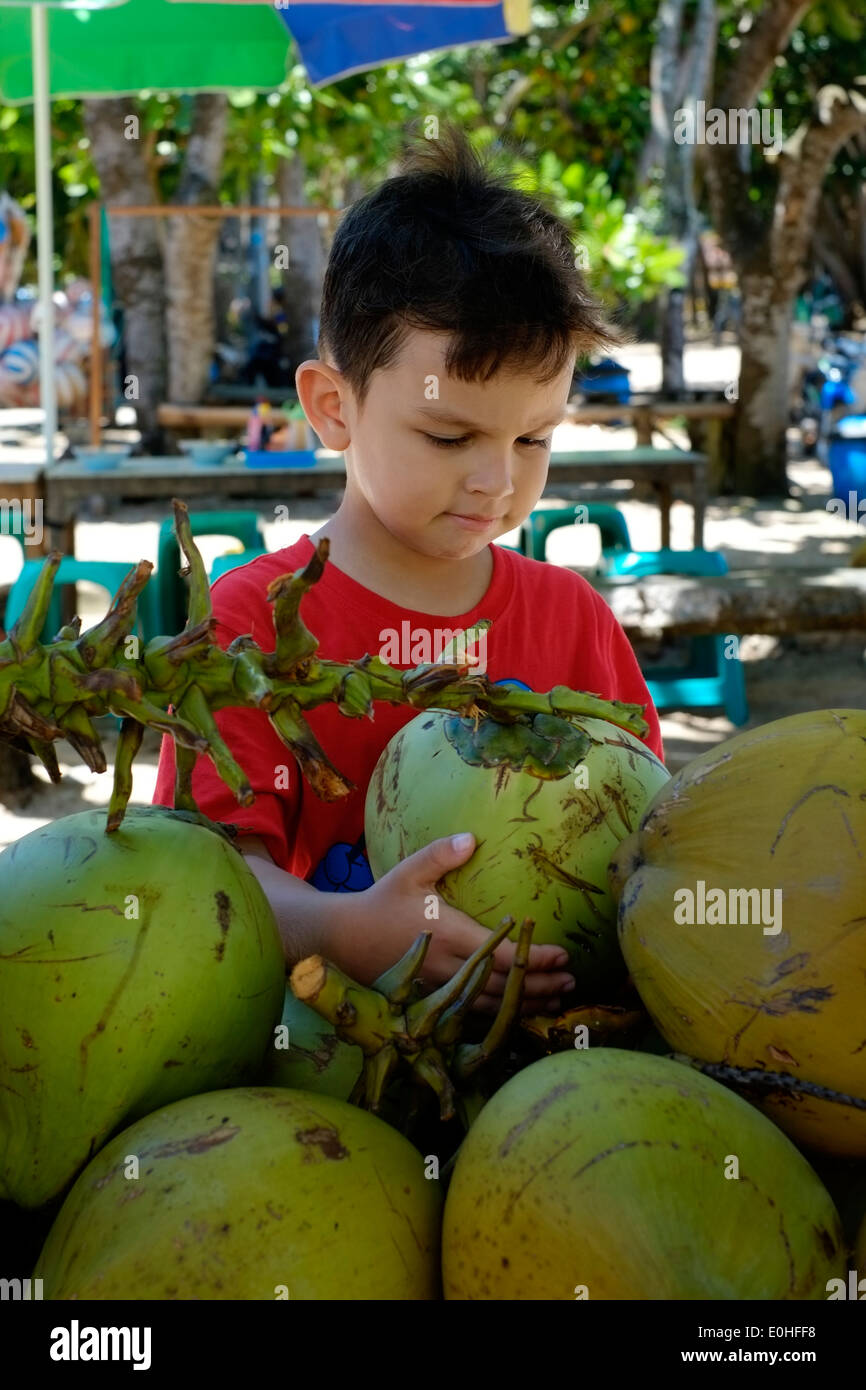 young boy looking at coconuts for sale by the beach and sea at ...