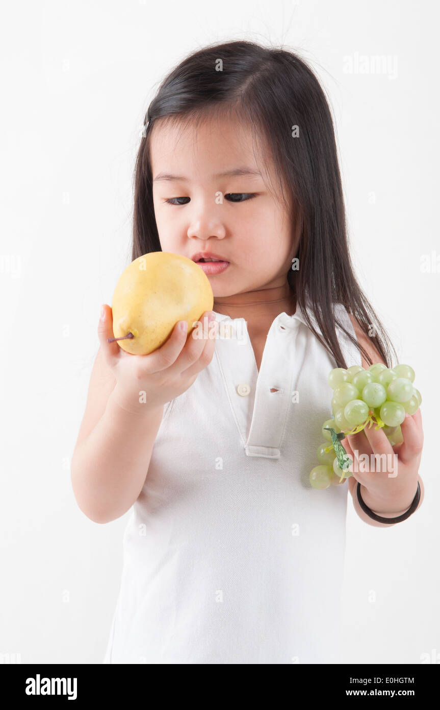 Child eats fruit. Little Asian girl eating pear and grapes, isolated on white background Stock ...