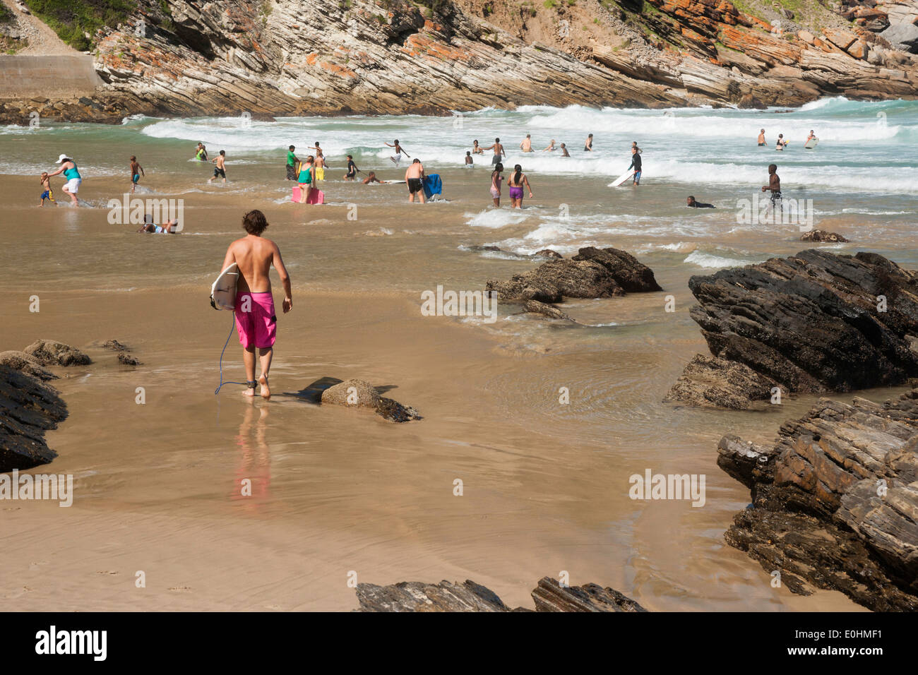 Beach scene with surfer walking on shore with swimmers in background ...