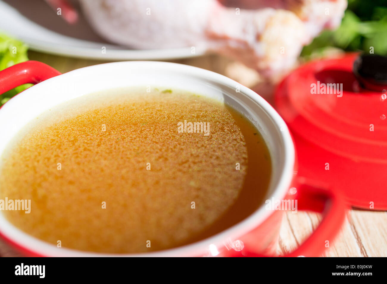 Chicken broth, bouillon, clear soup in a cup next to chicken and fresh ...