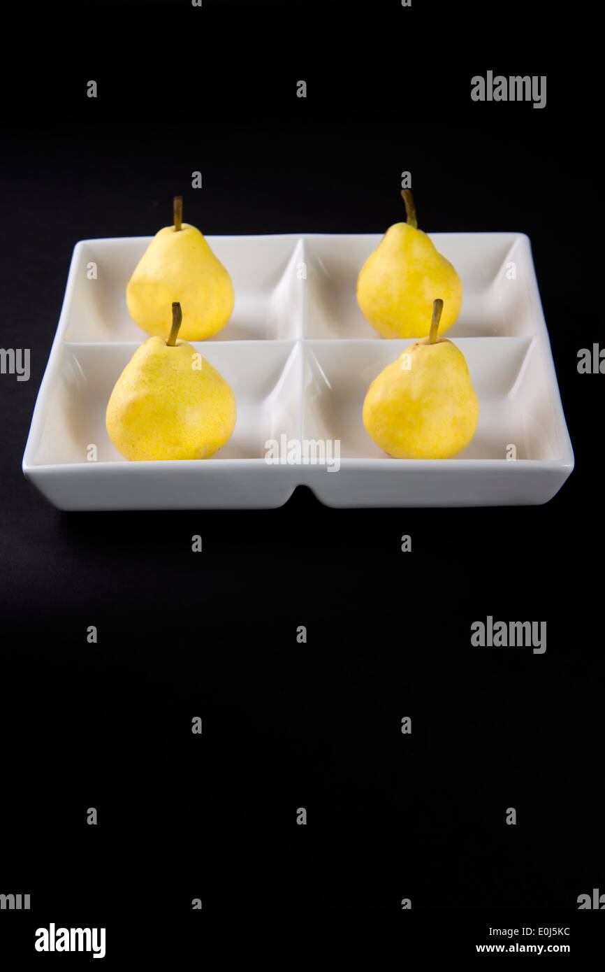 Four pears on a sectioned white china dish against a black background ...
