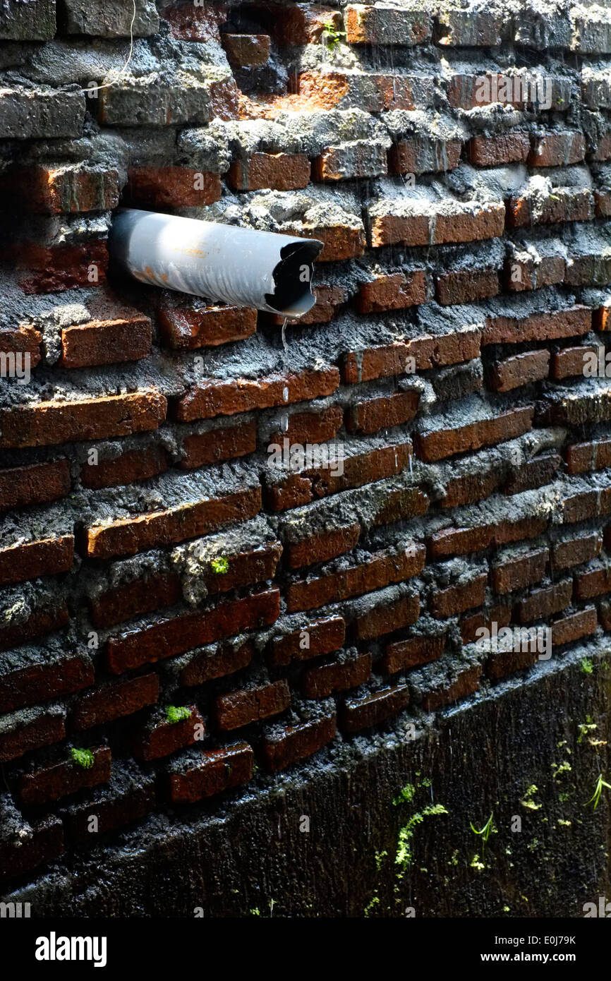 plastic water overflow drainpipe sticking out of wall drains water into a ditch below in rural ...