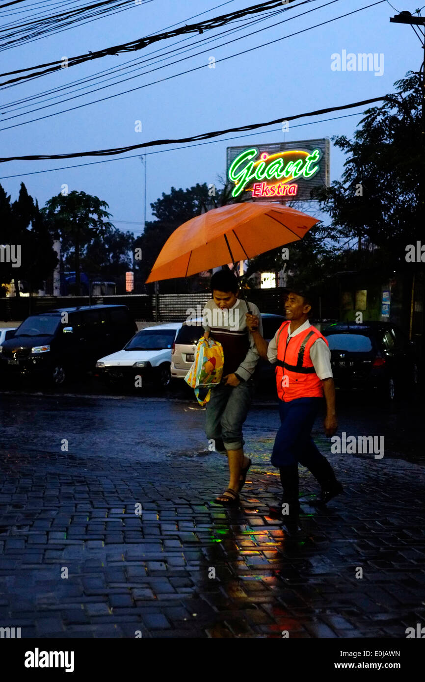 car park attendant shelters a man with umbrella as a deluge of monsoon ...