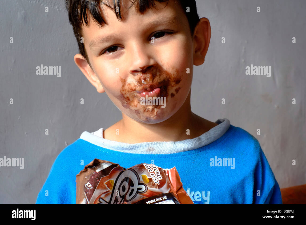 young boy eating a chocolate ice cream and getting most of it smeared ...