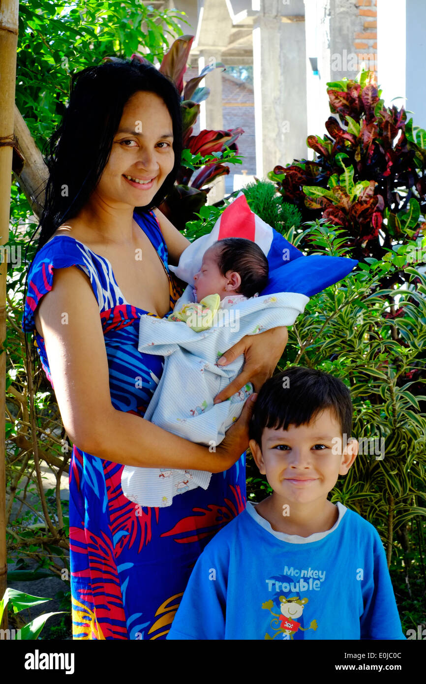 smiling new indonesian mother with her son holds her newborn daughter ...