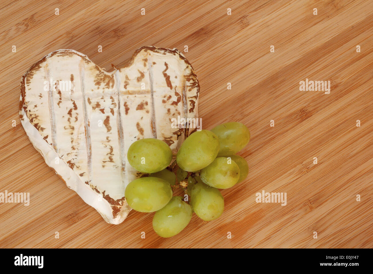 Neufchatel cheese shaped like heart with grapes on wooden cutting board ...