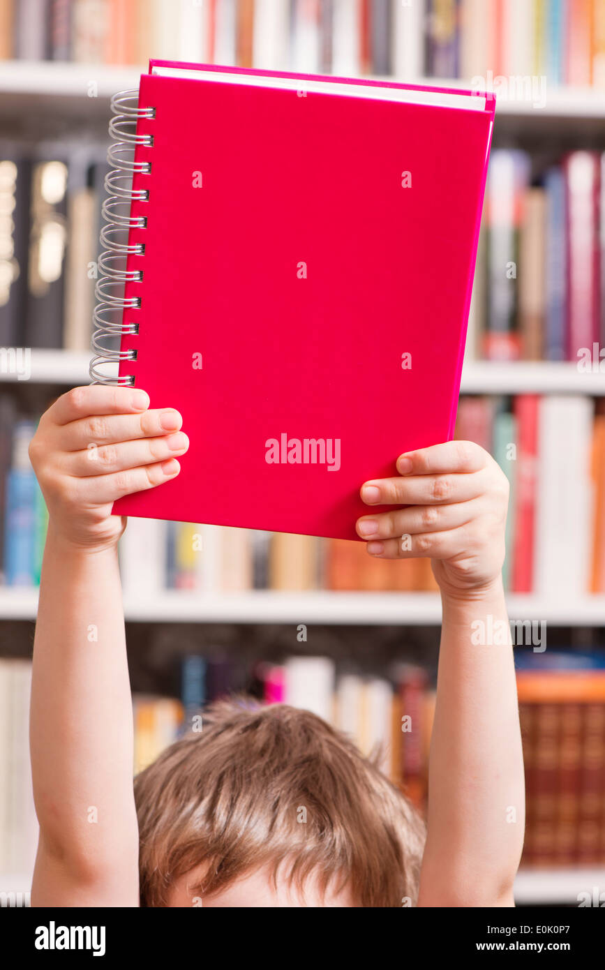Young child holding red book over head in a library Stock Photo - Alamy