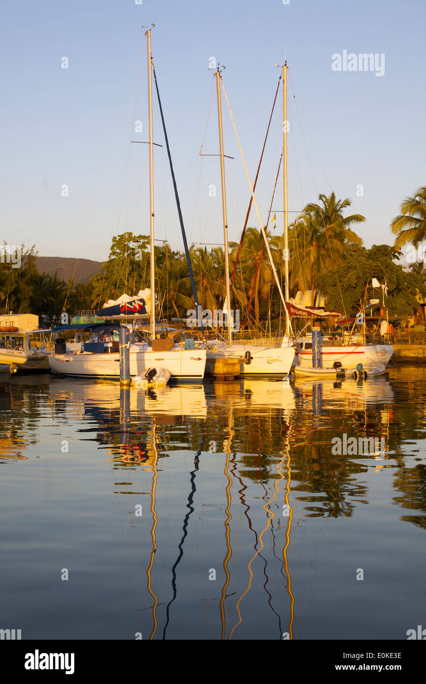 Sailboats docked at a yacht club reflect in the calm water at sunset ...