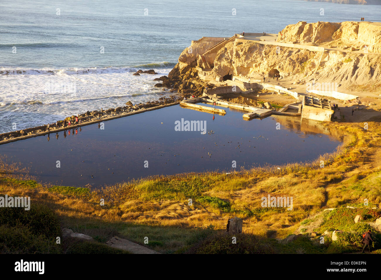 People walk in a single file line along the sea wall at the Sutro Bath ...