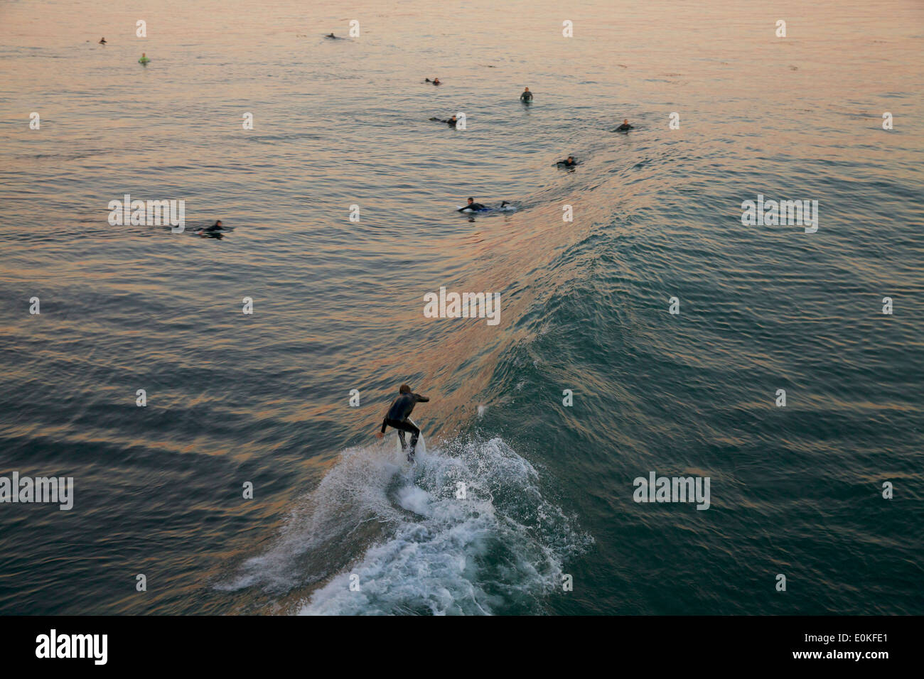 A view from behind of a surfer catching a wave as other surfers watch ...