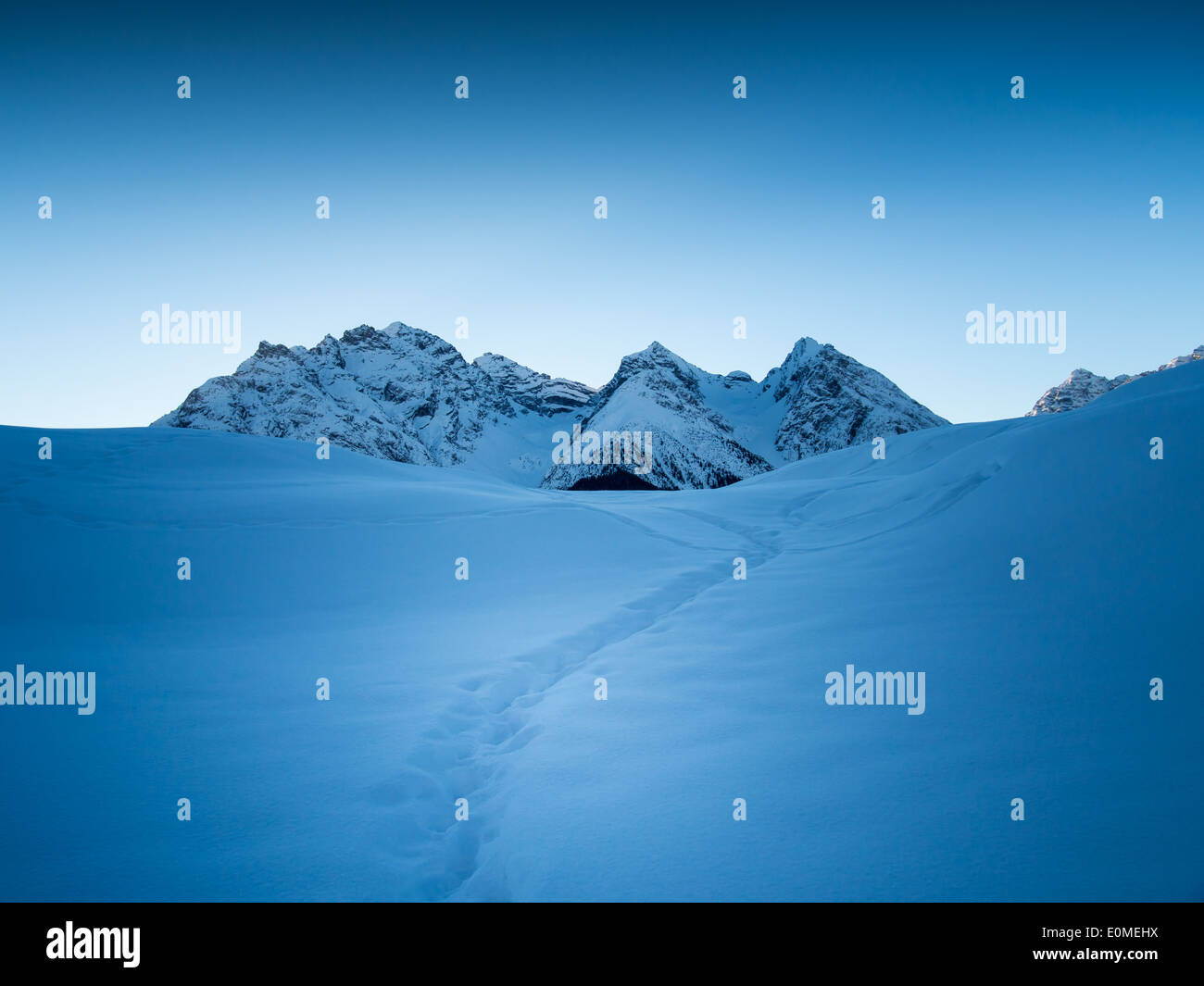 A path leads through the fresh snow in the Swiss Alps, early in the ...