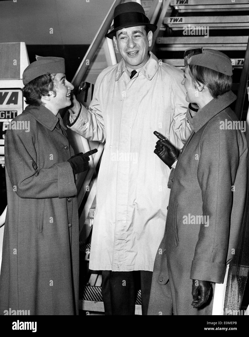 Actor Shelley Berman talking with two hostesses before boarding Stock ...