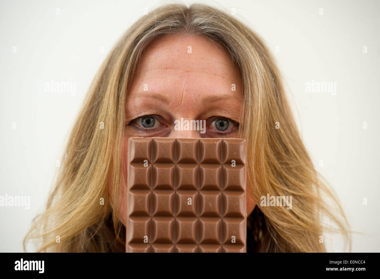 A middle-aged lady holding a bar of chocolate in front of her face ...