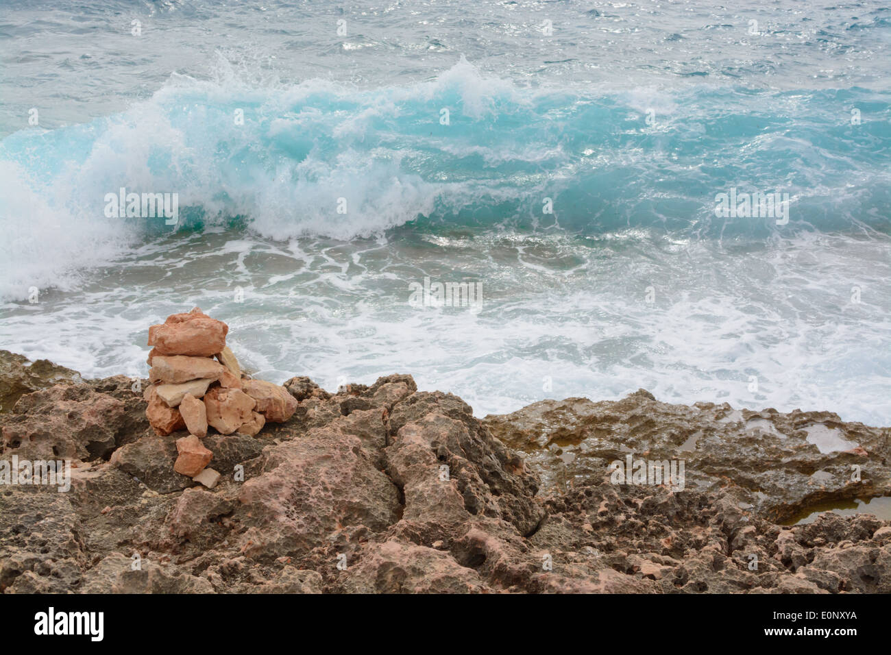 Turquoise wave splashing onto little stone tower and shore at Cap de ...