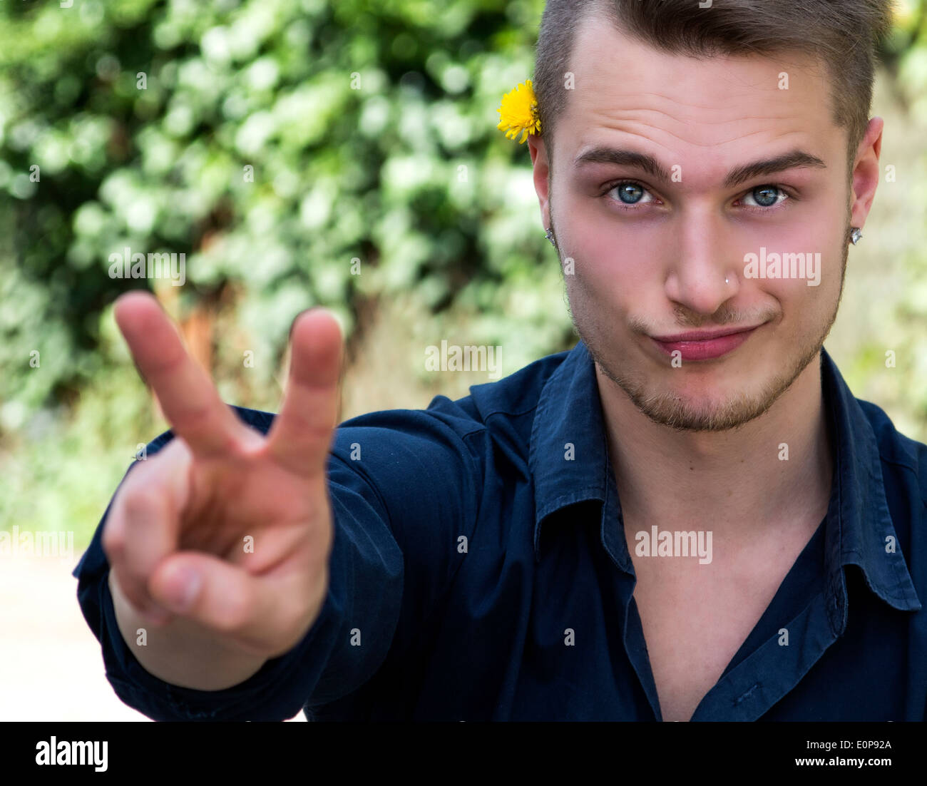 Handsome blond young man outdoors in nature doing peace sign with ...
