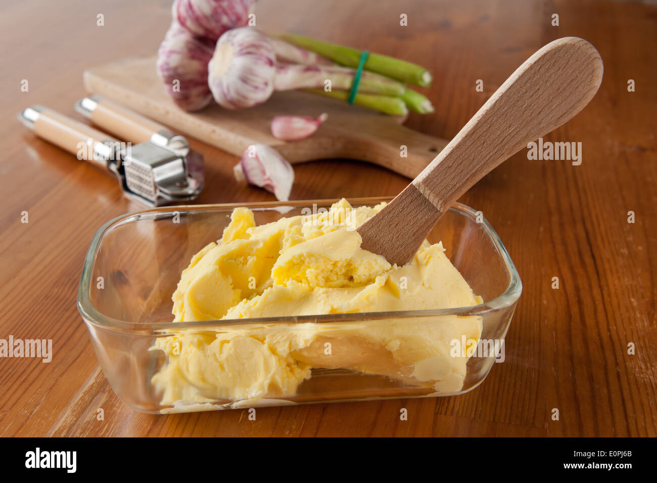 Glass butter dish and garlic, open container and wooden knife in butter ...