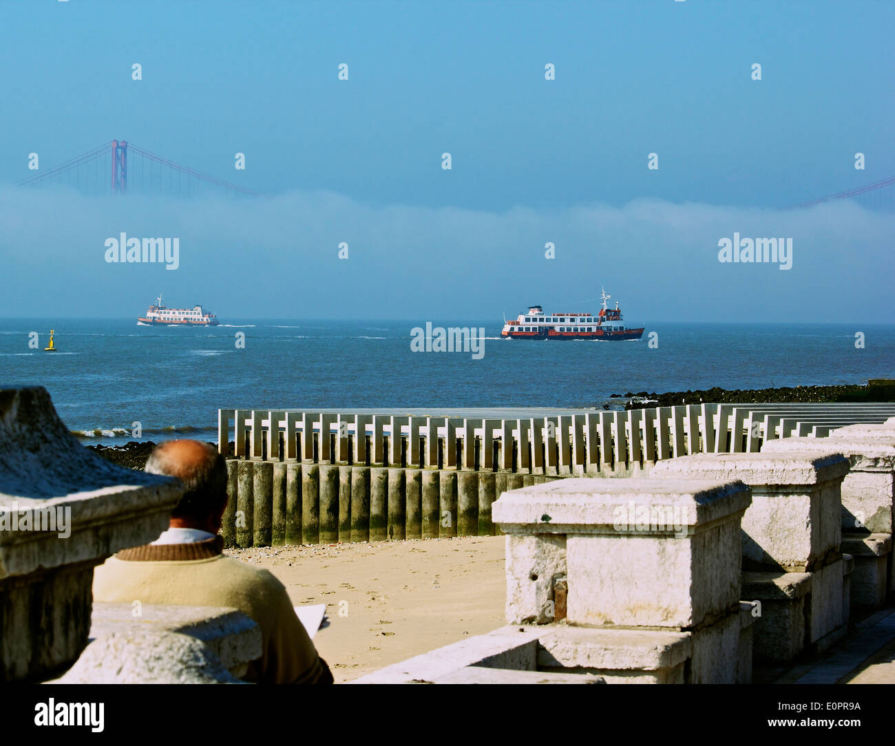 Man sitting relaxing by river Tagus (Tejo) with two ferries crossing ...
