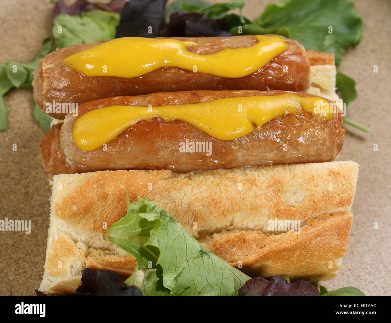Grilled sausages on a crusty baguette with mustard and salad garnish ...