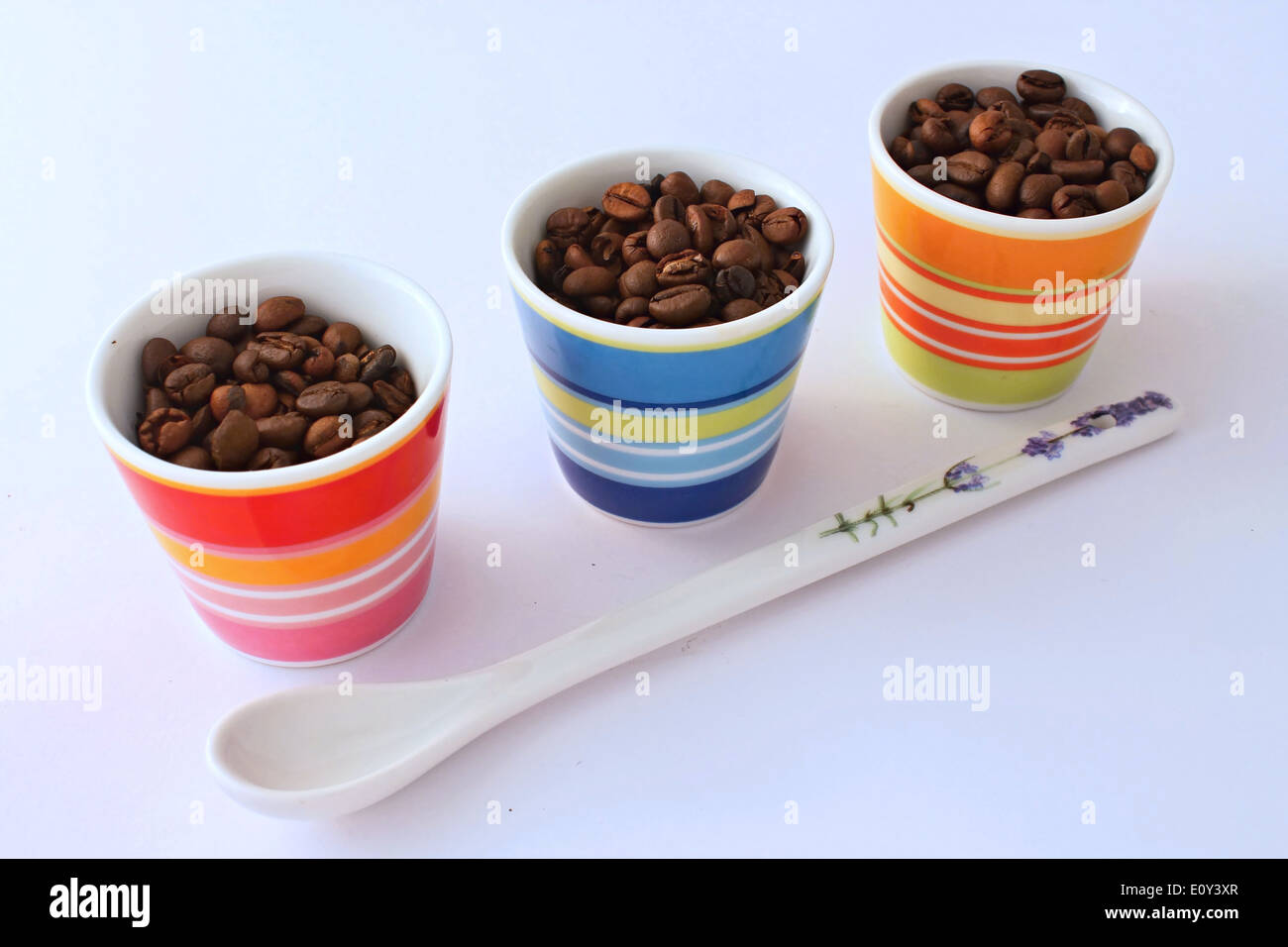 Three color cups with coffee grains and ceramic spoon Stock Photo - Alamy