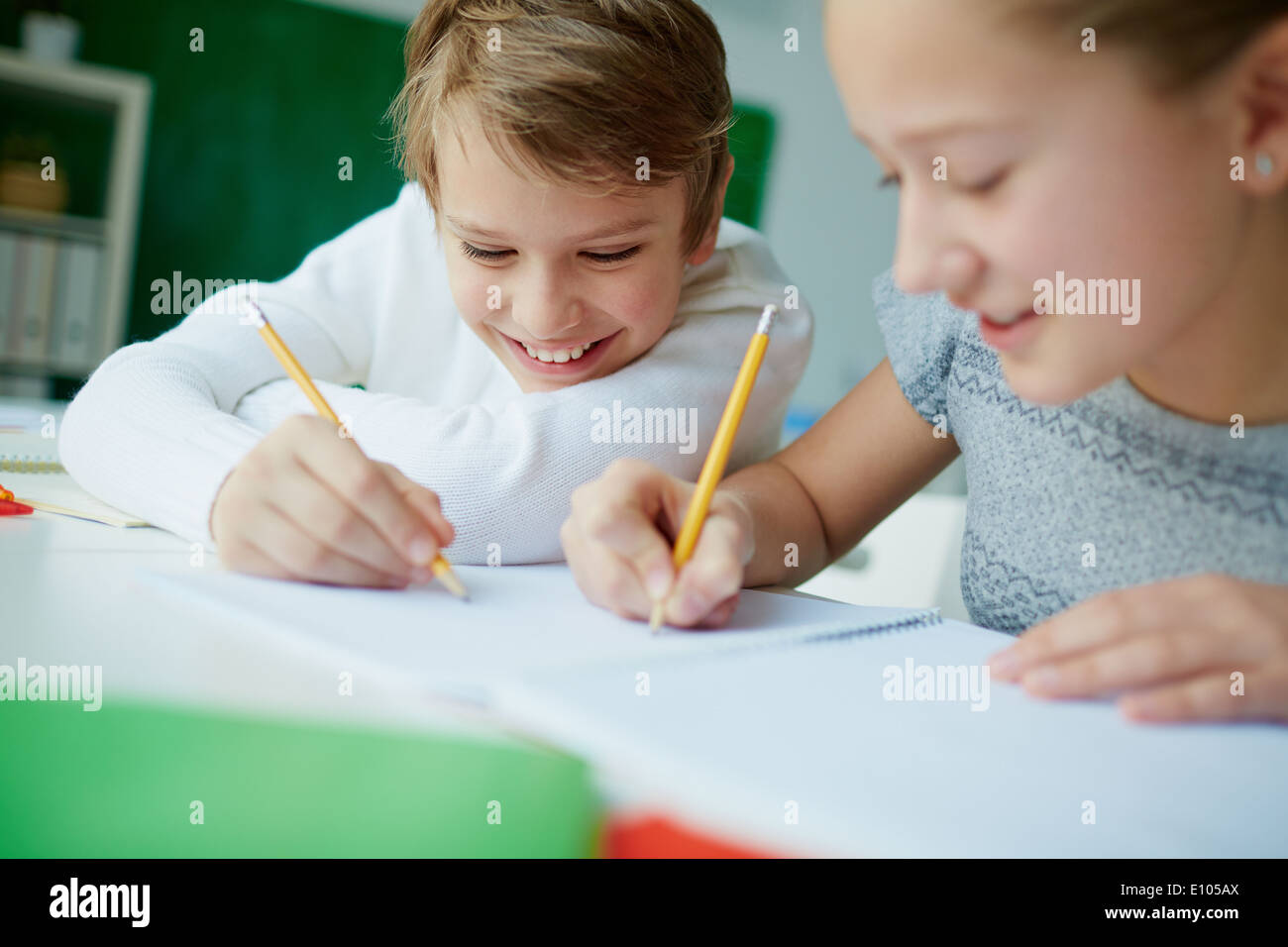 Portrait of cute schoolboy drawing at lesson with his classmate near by ...