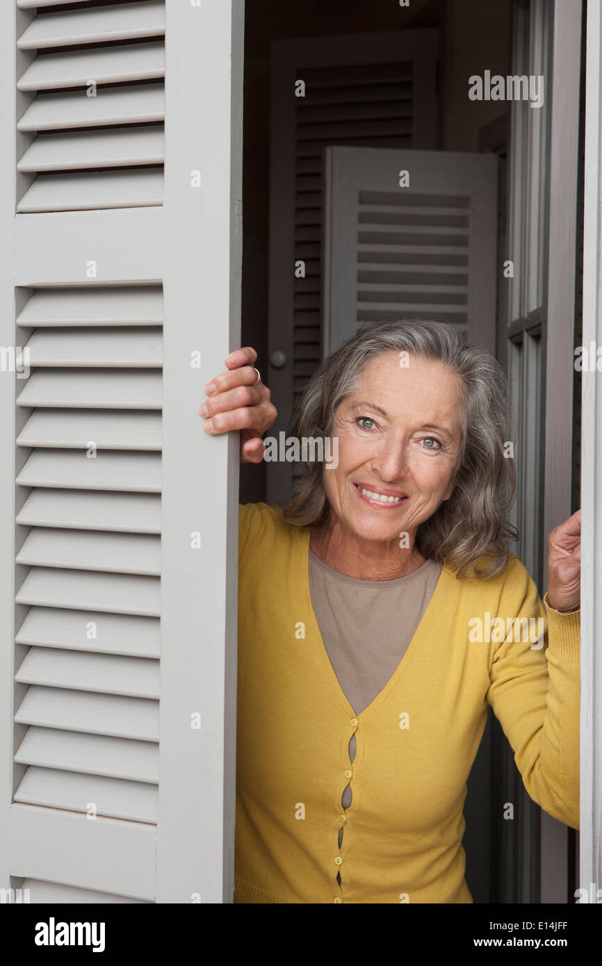 Woman peering out window shutters Stock Photo - Alamy
