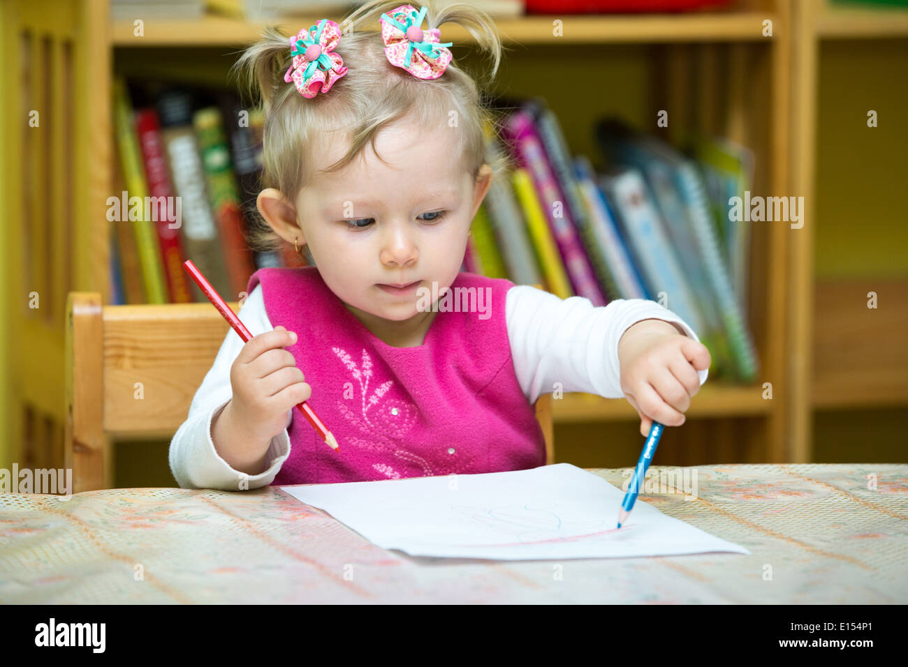 Cute child girl drawing with colorful pencils in preschool at the table ...