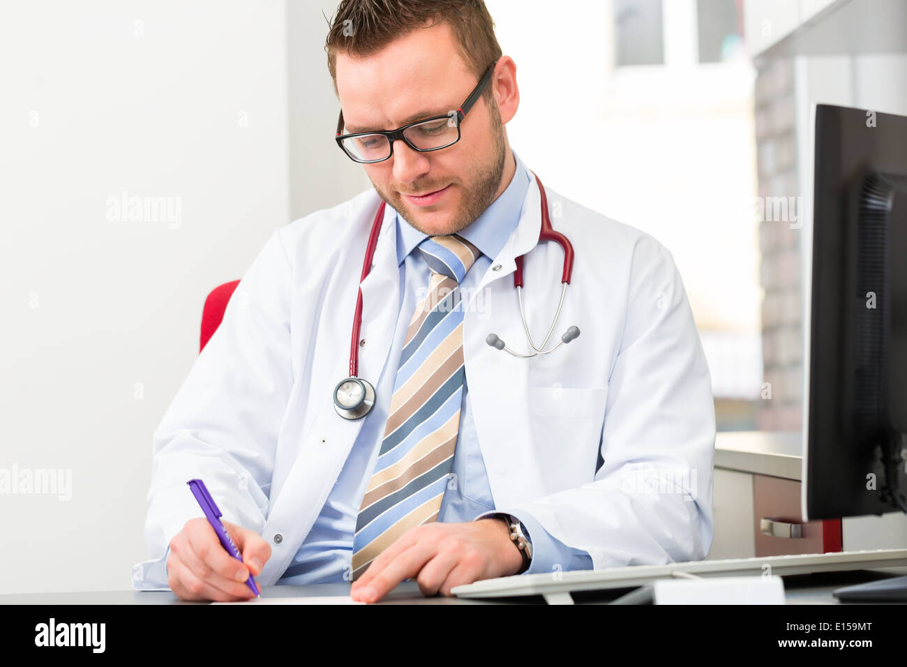 Young doctor writing medical prescription in surgery at desk Stock ...