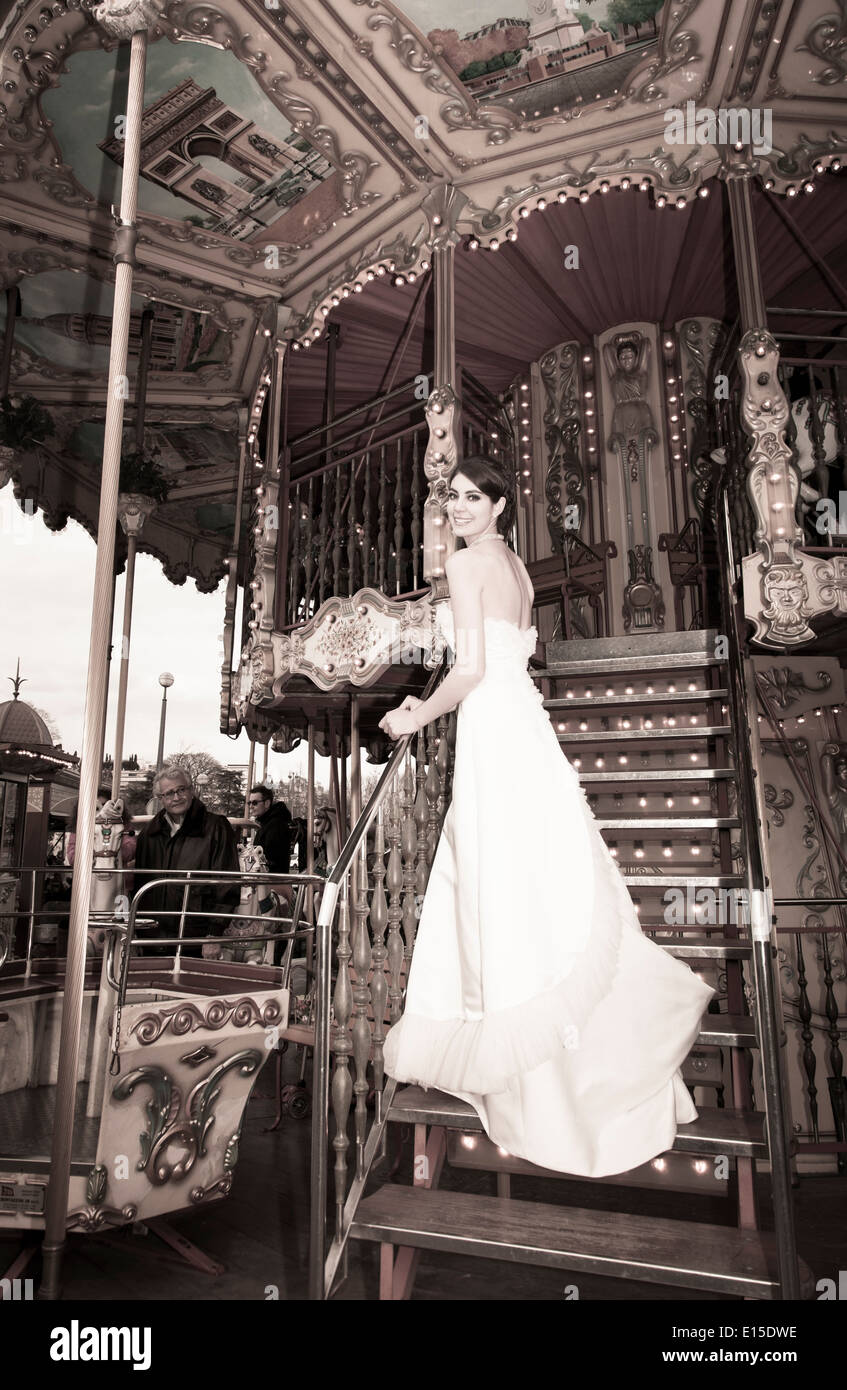 Young woman wearing wedding dress standing on steps of an old carousel ...
