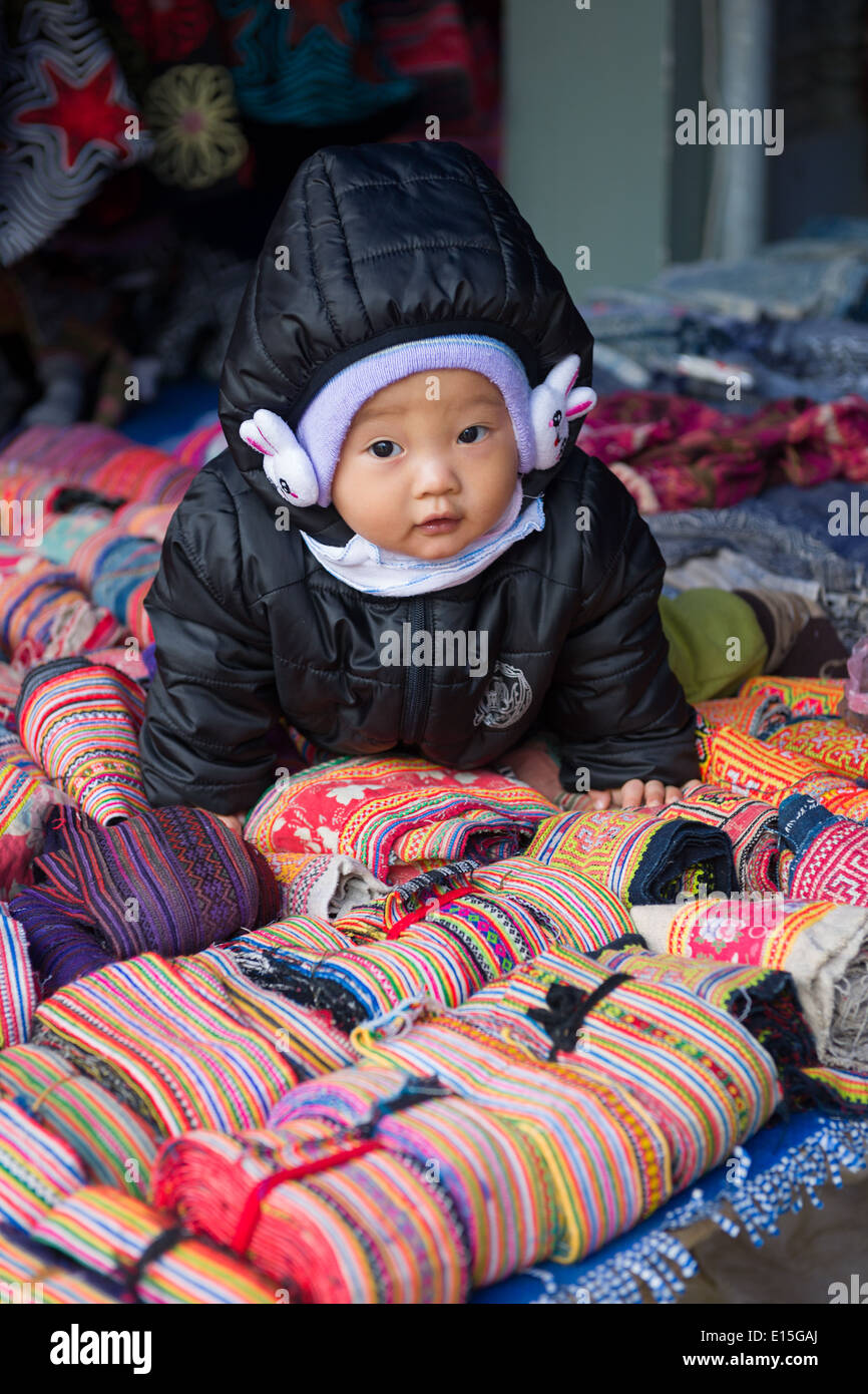Small child crouching on a pile of Flower Hmong weaving, Bac Ha Market ...