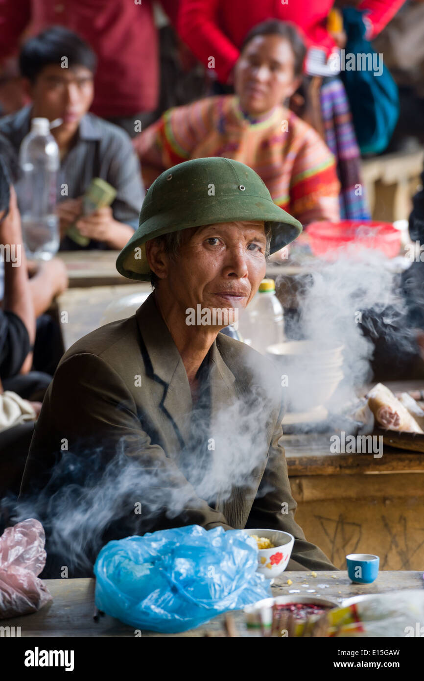 Hmong man in a Vietnamese Army helmet exhaling smoke whilst sitting in ...