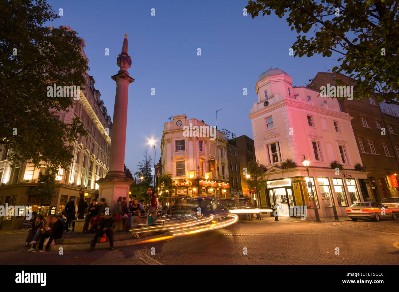 Traffic passing people sitting on the sundial pillar monument at dusk ...