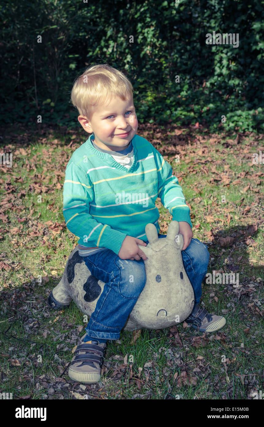Young cute little boy sitting on toy cow in the garden outside Stock ...