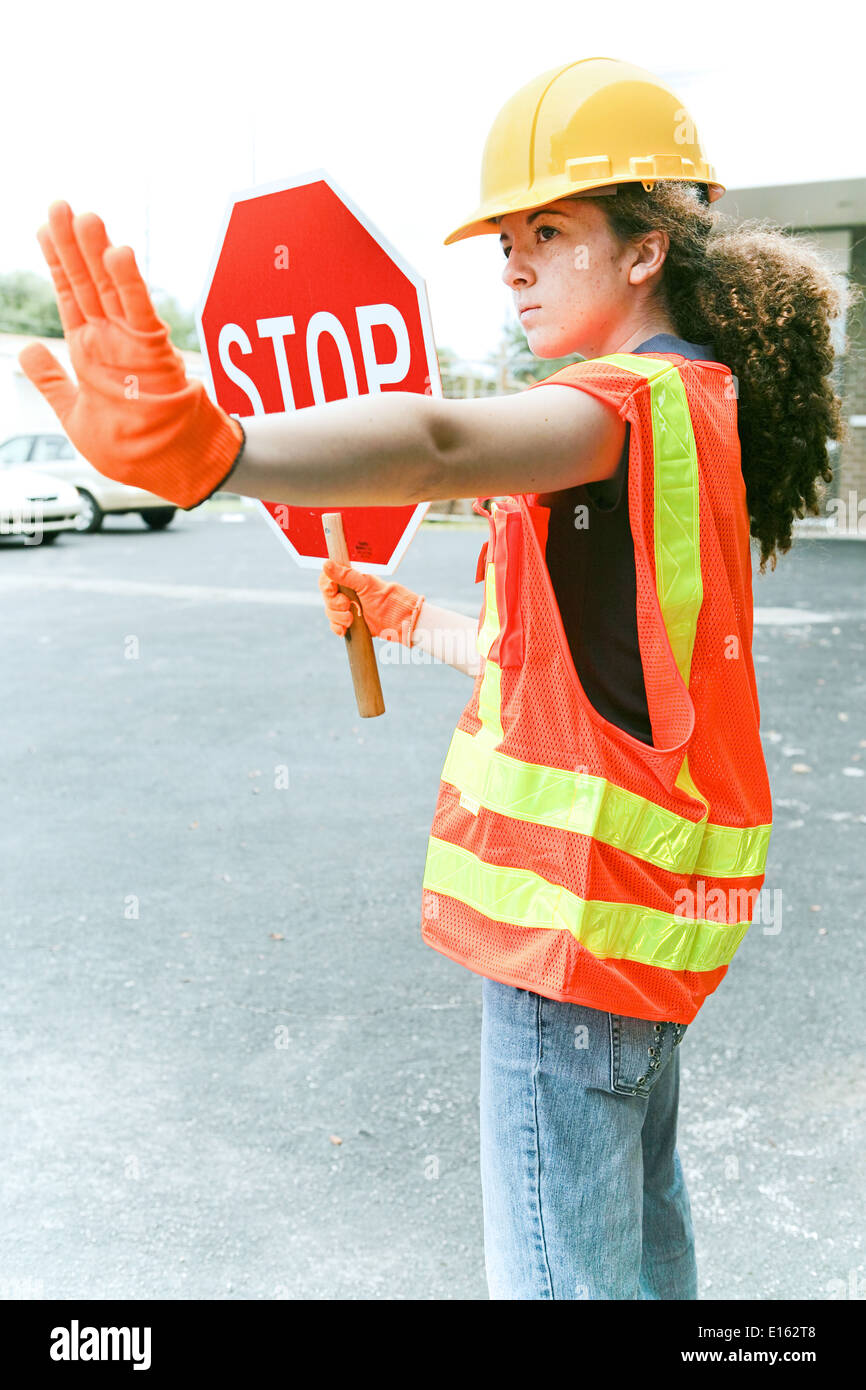 Young female construction apprentice holding a stop sign and directing ...