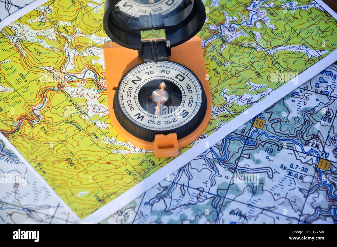 Open magnetic compass with mirror cover is lying on a topographic map ...