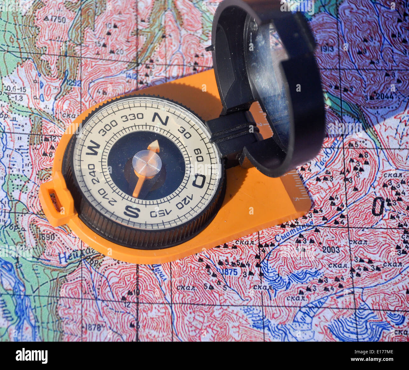 Open magnetic compass with mirror cover is lying on a topographic map ...