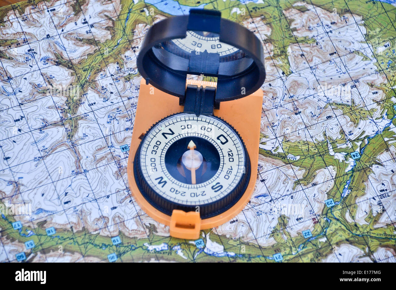 Open magnetic compass with mirror cover is lying on a topographic map ...