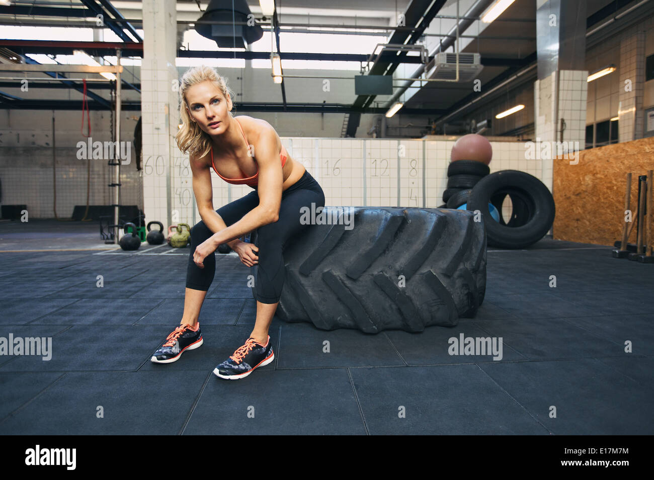 Fit young lady sitting on a big tire after her workout. Woman taking ...