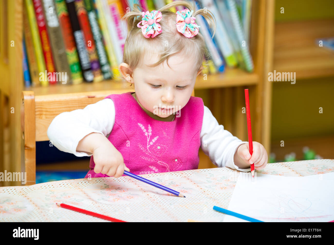 Cute child girl drawing with colorful pencils in preschool at the table ...