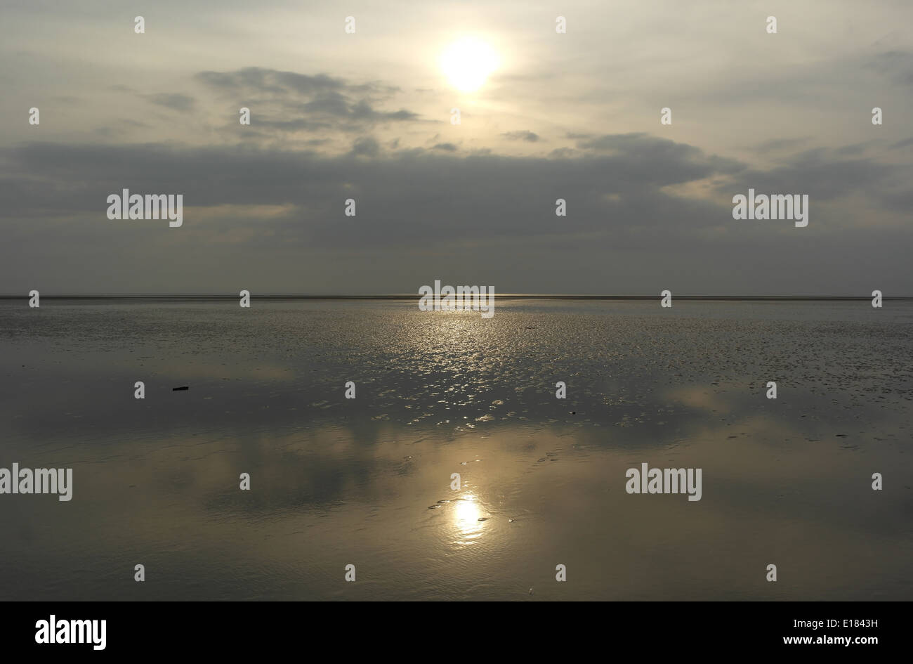 Sun setting below grey clouds with reflections in wet sand pools on the ...