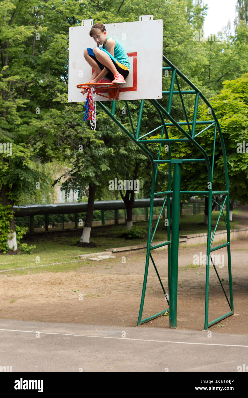 Young teenage girl fixing a basketball net sitting crouched on the hoop ...