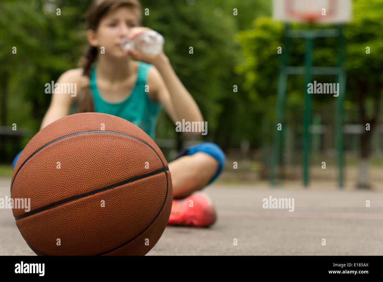 Young basketball player drinking water as she sits cross-legged on the ...